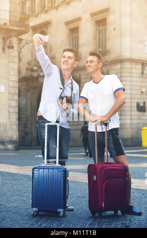 Two positive european men with luggage doing selfie during city tour at ...