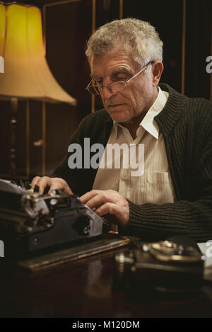 Pensive Retro Senior Man writer with glasses in his hand, sitting at ...