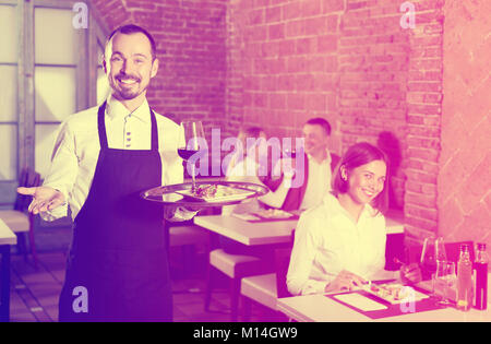 Positive male waiter showing country restaurant to visitors Stock Photo ...