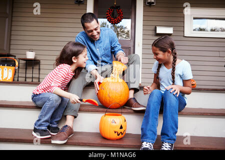 Father and three children carving Halloween pumpkins in the garden ...