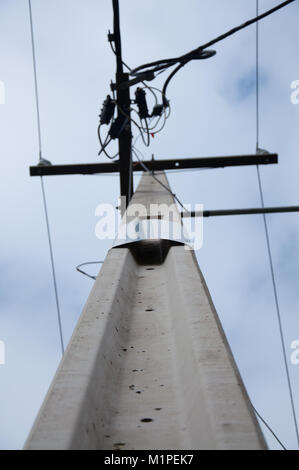 Looking up at concrete power pole and powerlines against clear blue sky ...