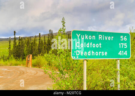 A muddy road with a street sign and a mountain landscape covered with ...
