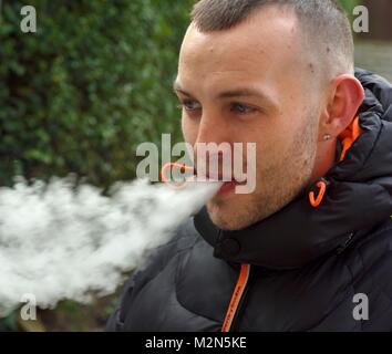 Young man vaping smoking an e-cigarette with a cloud of smoke obscuring ...