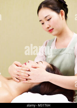 Woman therapist performing a facial massage on a female client lying on ...