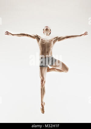 Athletic ballet dancer in a perfect shape performing over dark studio ...