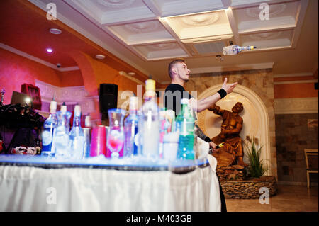 Talented bartender performing tricks with bottles and glasses in front ...