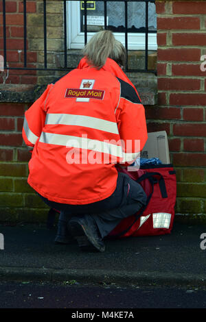 A female Royal Mail postal worker delivering post to a house on her ...