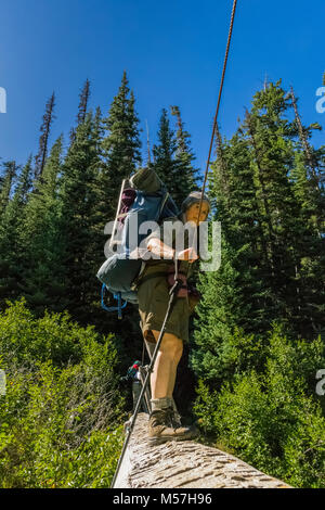 Backpacker crossing a log over a stream in Oregon's Wallowa Mountains ...