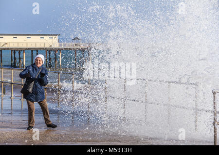 Woman avoiding being splashed by a wave at high tide on the promenade ...