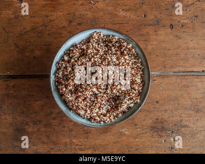 A bowl of cooked red and white quinoa on a rustic wood table ...