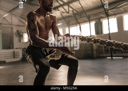 Strong man pulling heavy rope at cross training gym. Male athlete doing ...