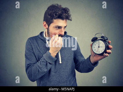 Young man scared of time holding clock Stock Photo - Alamy