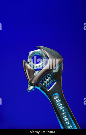 Extreme closeup of adjustable wrench gripping a screw nut on blue ...