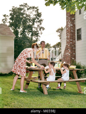 1960s SUBURBAN FAMILY OF FOUR AT PICNIC TABLE IN BACKYARD EATING Stock ...