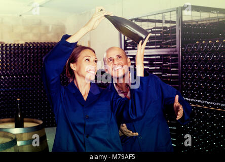 Two glad winery workers holding bottle of sparkling wine in aging ...