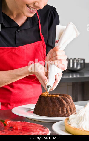 Female happy baker squeezing whipped cream from pastry bag on tasty ...