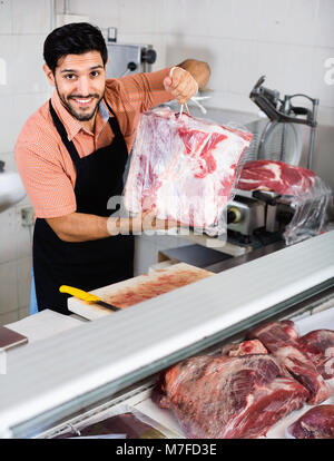 Smilling happy cheerful butcher is offering meat to clients in market ...