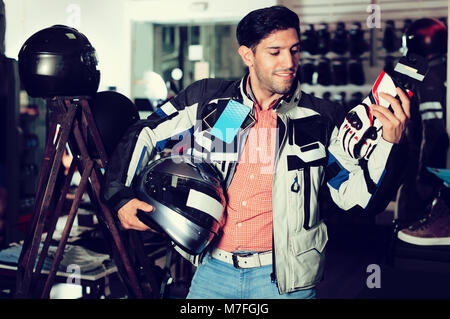 Smiling man is choosing moto helmet for head protection in sport shop ...