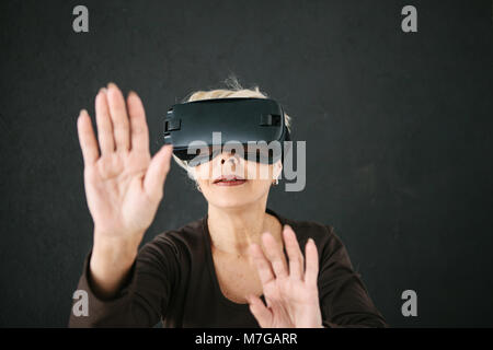 Aged female in futuristic glasses standing under neon illumination in ...