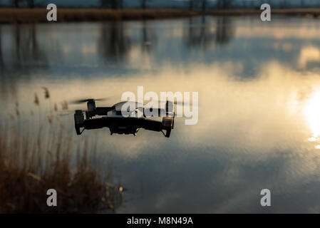 Small modern drone taking picture of lake at sunset Stock Photo - Alamy
