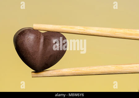Chinese chopsticks holding a chocolate candy on a yellow background ...