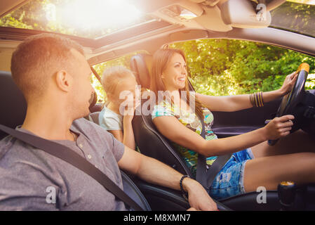 Beautiful family of three enjoying at driving a car and going on road ...