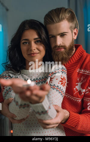 Young couple in Christmas sweaters and Santa hats on color background ...
