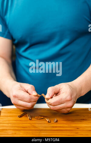 Man breaking a cinnamon stick over a wooden board Stock Photo - Alamy