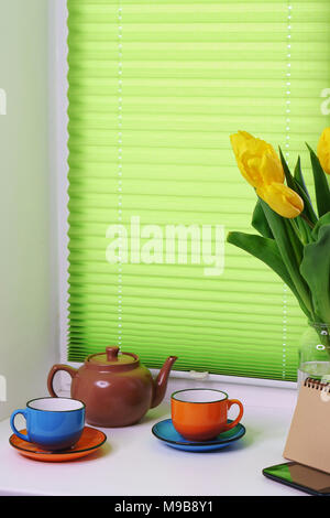 Teapot, cups, tulips and greeting card on dining table in kitchen ...