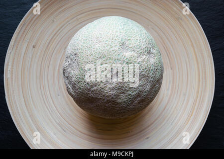 Full head of Hami melon fruit on brown straw mat background surface ...