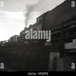 1950s, historical, a steam locomotive on a railway line, emerging from ...