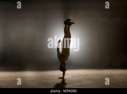 Teenager doing an acrobatic one-arm handstand on a jetty at the beach ...