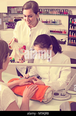 happy manicurists choosing color of nail polish with client in nail ...