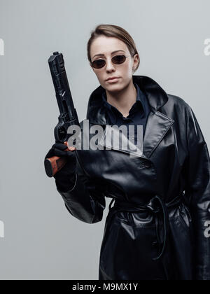 Cool female spy agent in black leather coat, she is holding a gun and ...