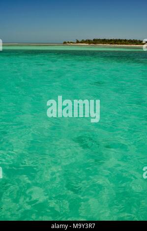 Distant white sandy beach-rimmed island with clear blue sky and ...
