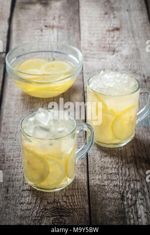 Two cups of lemonade and ice cubes crumbs on a wooden table background ...