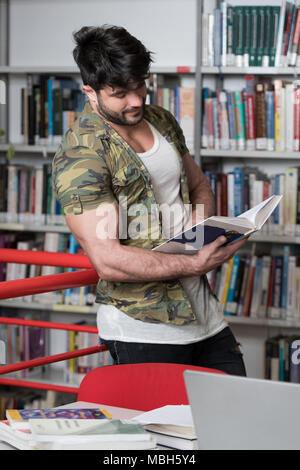 Muscular young man standing reading book with surprised expression ...