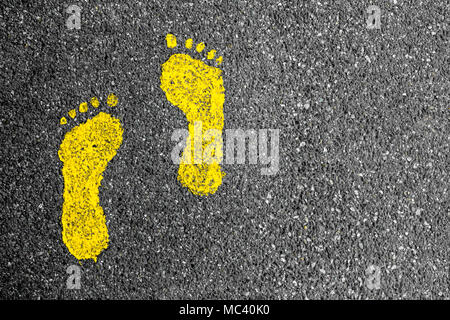 Yellow footprint signs on an asphalt road. Painted footprints show the ...