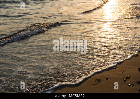 Waves approaching beach sand during golden sunset Stock Photo - Alamy