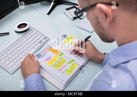Businessman's Hand Writing Schedule In Diary With Pen At Workplace ...