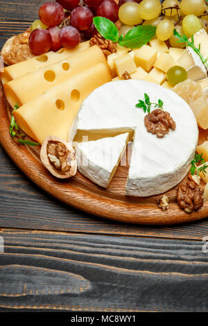 Wooden cutting board with cheese variety on dark concrete background ...