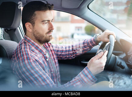 Young driver guy distracted by his phone while in front of the steering ...