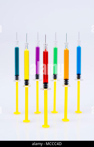 Multiple syringes with needles, filled with various colours of medicine ...
