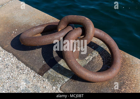 Rusty metal dock ring with mooring rope tied at marina pier near calm ...