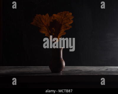 Autumn bouquet. Dry oak leaves in a clay vase. Photo on a black ...