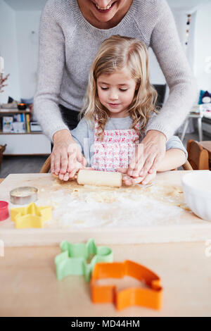 A girl is using the rolling pin to roll out the dough on the table ...