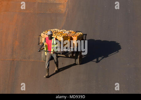 A Kenyan man pulling a handcart along a road carrying plastic chairs on ...