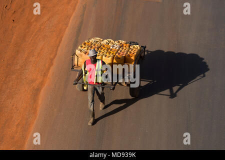 A Kenyan man pulling a handcart along a road carrying plastic chairs on ...