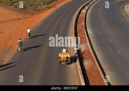 A Kenyan man pulling a handcart along a road carrying plastic chairs on ...