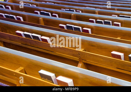 Rows of pews in a church have book shelves holding Bibles and pews ...